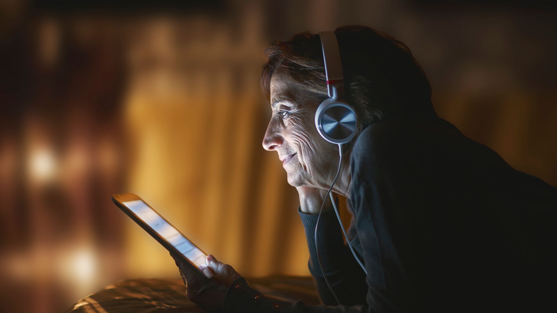 Ratio 16_9-Older woman on bed reading tablet with headphones - Vodafone ...